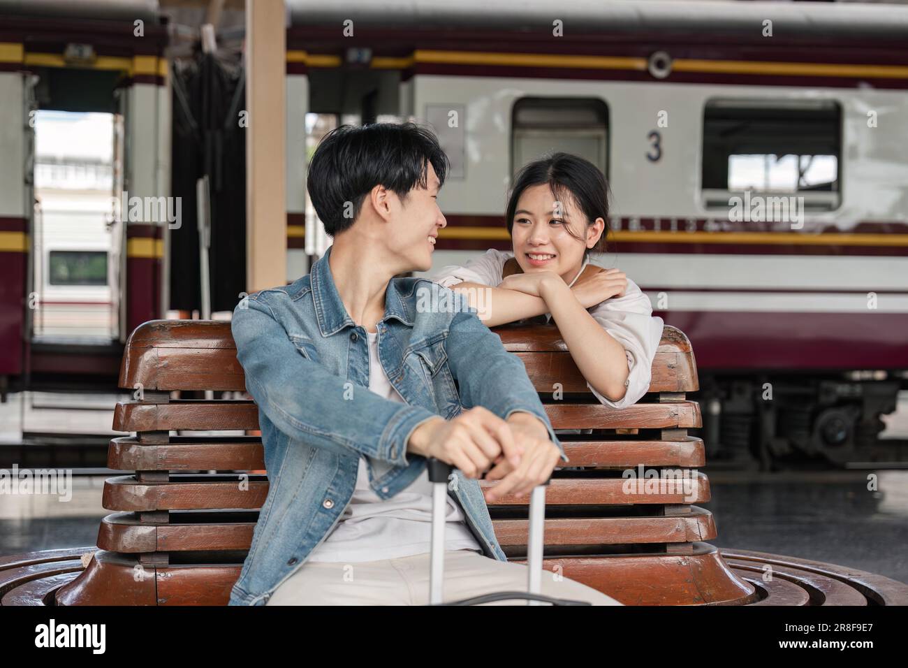 Young couple sitting on wooden bench at train station. Couple sitting ...