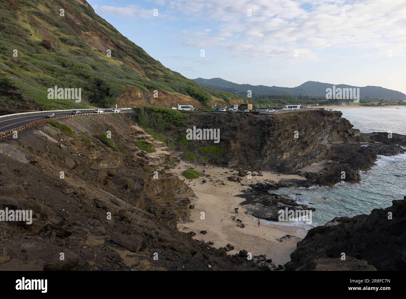 A scenic view of a road in a coastal landscape, with several cars and ...