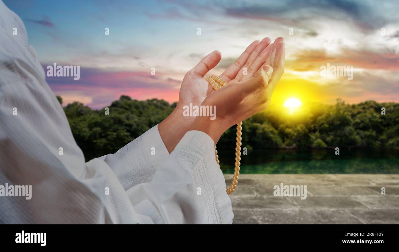 Muslim man praying with prayer beads in his hands with the sunset scene ...