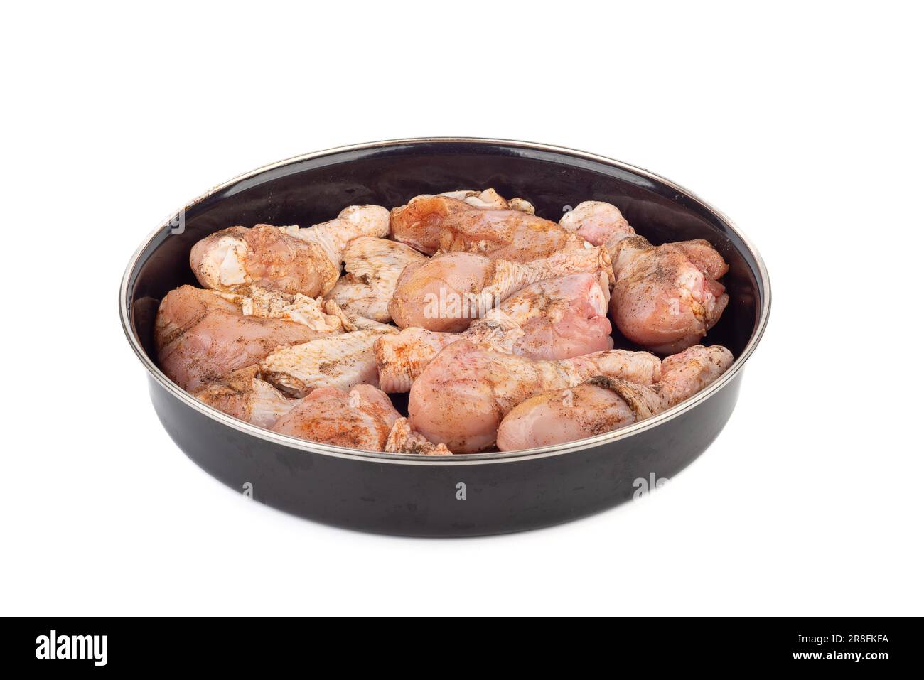 Ready-to-bake chicken drumsticks in a round metal mold over a white ...