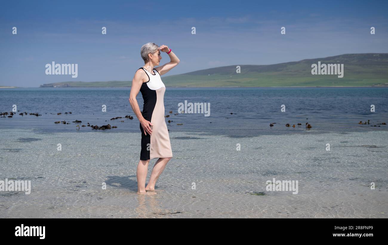 Woman in a smart dress walking barefoot along a sandy beach in the ...