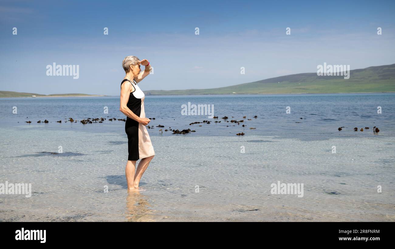 Woman in a smart dress walking barefoot along a sandy beach in the ...