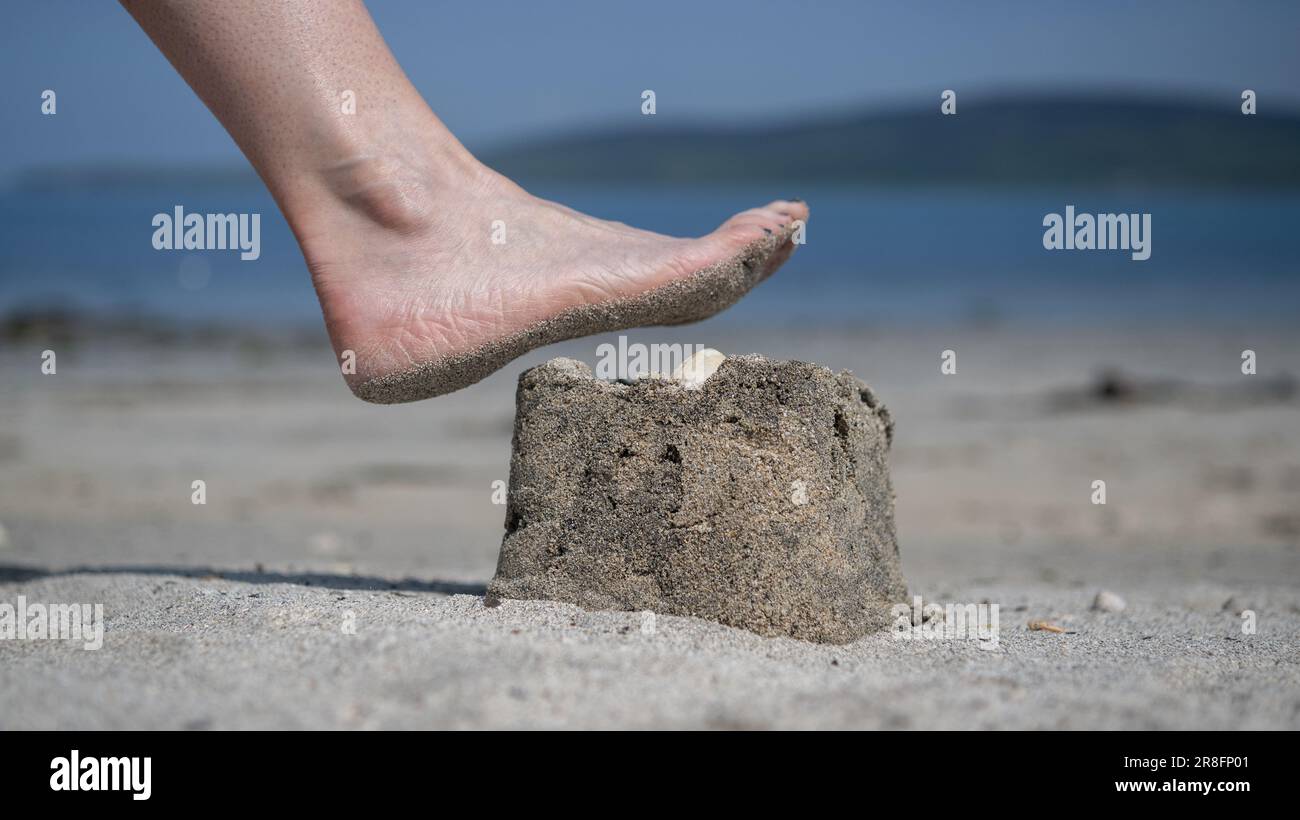 Persons barefoot about to stand on and flatten a sandcastle on the ...