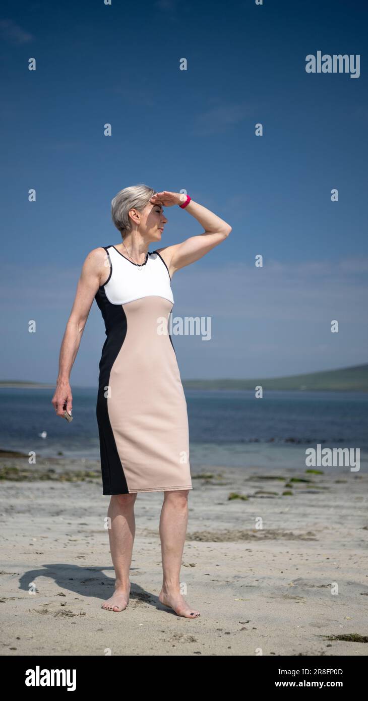Woman in a smart dress walking barefoot along a sandy beach in the ...