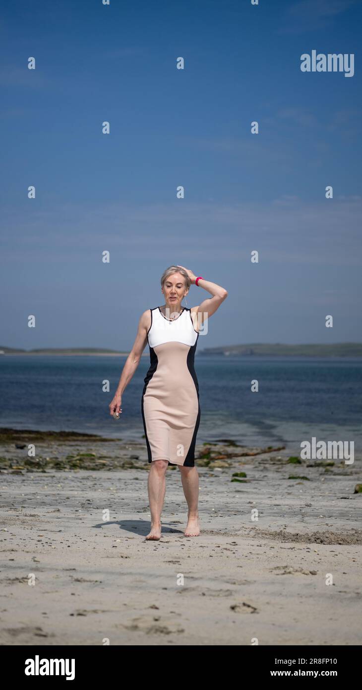 Woman in a smart dress walking barefoot along a sandy beach in the ...