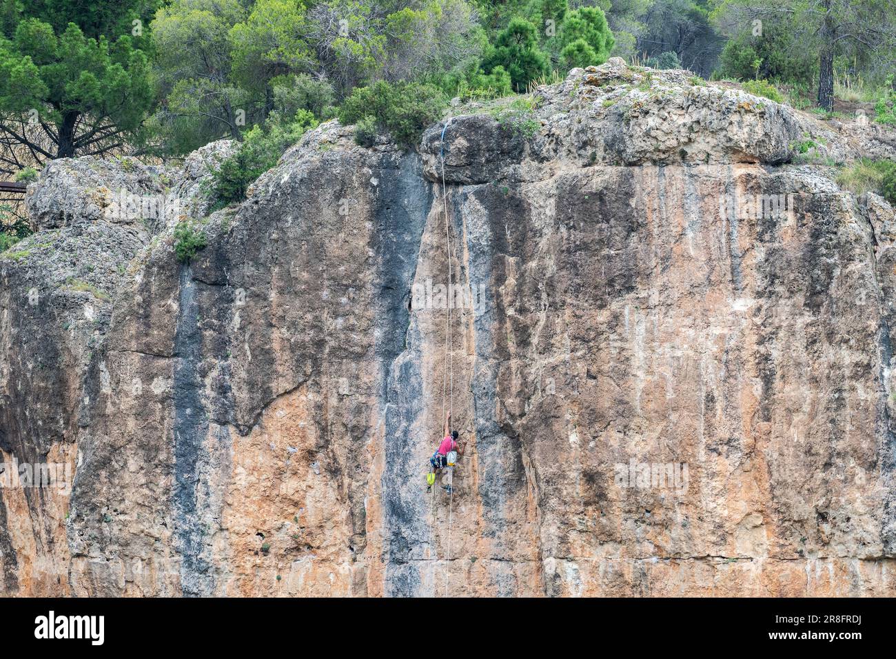 A man hanging by a rope climbs a vertical rock wall in a canyon above ...