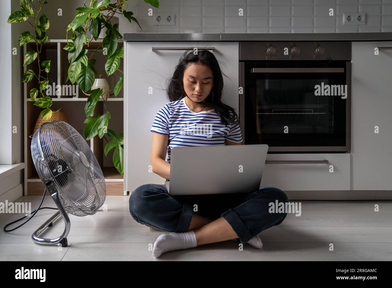 Focused Asian woman turn on floor ventilator fan while work with laptop ...