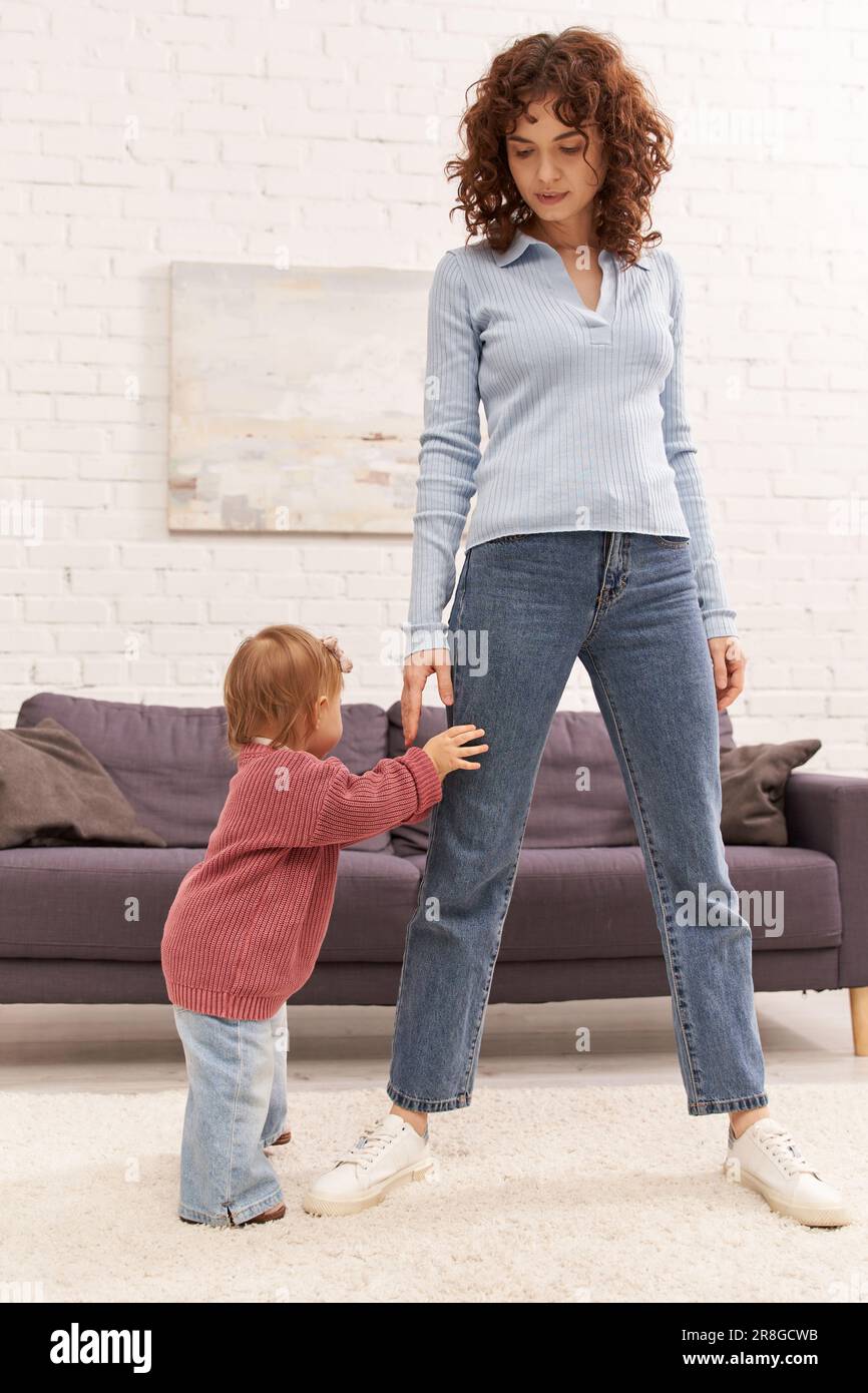 full length of toddler baby doing her first steps near curly mother ...