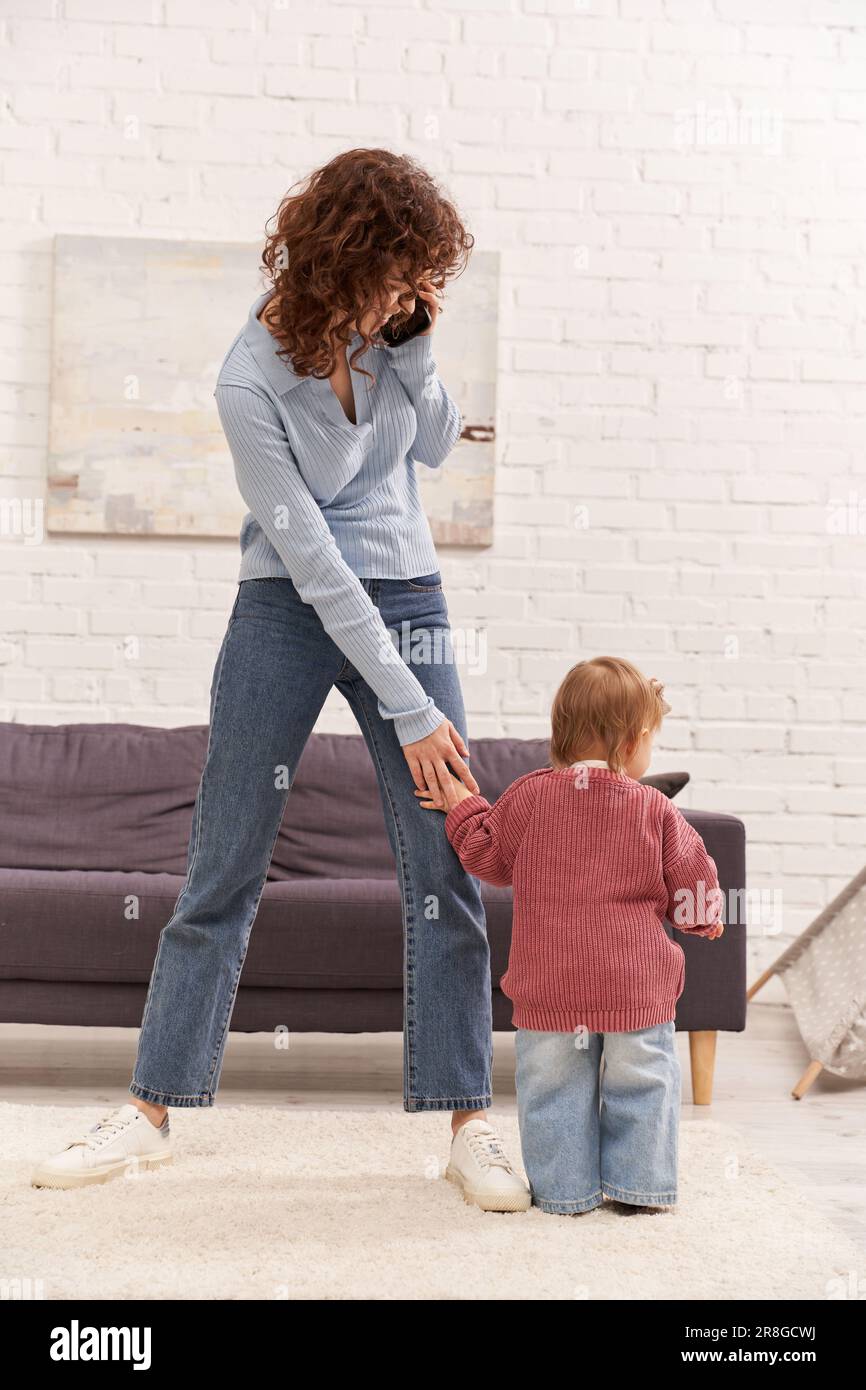 full length of toddler baby doing her first steps near curly mother ...