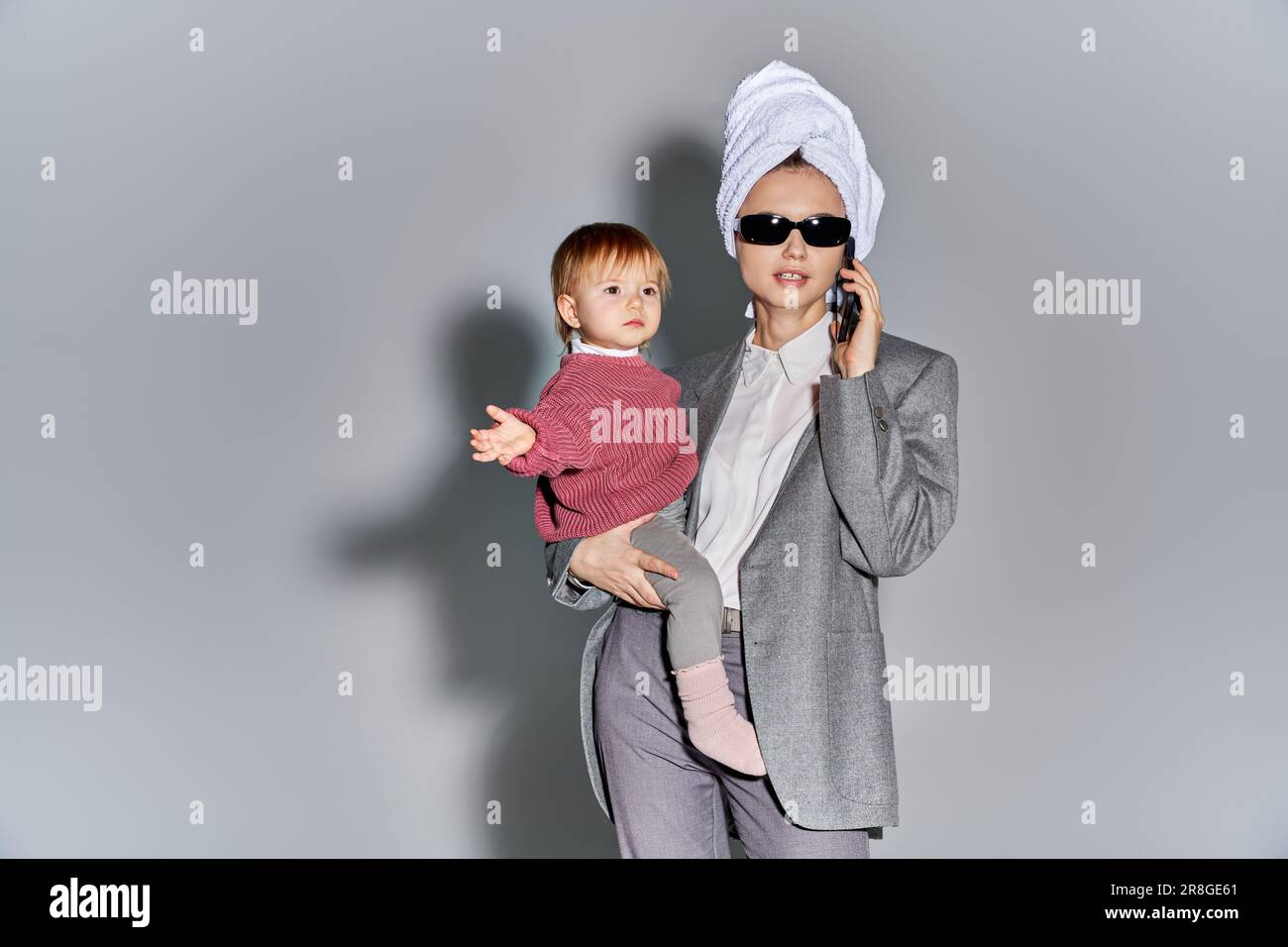 multitasking, woman in sunglasses holding in arms toddler daughter and ...