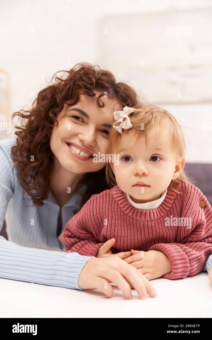 portrait of cheerful woman and child, curly working mother hugging baby ...
