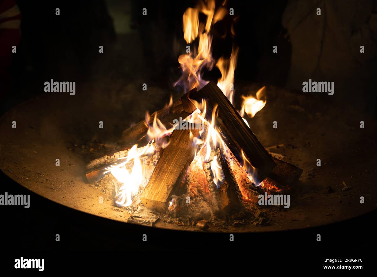 A fire in a fire pit in the dark, with some burned sticks in the embers ...