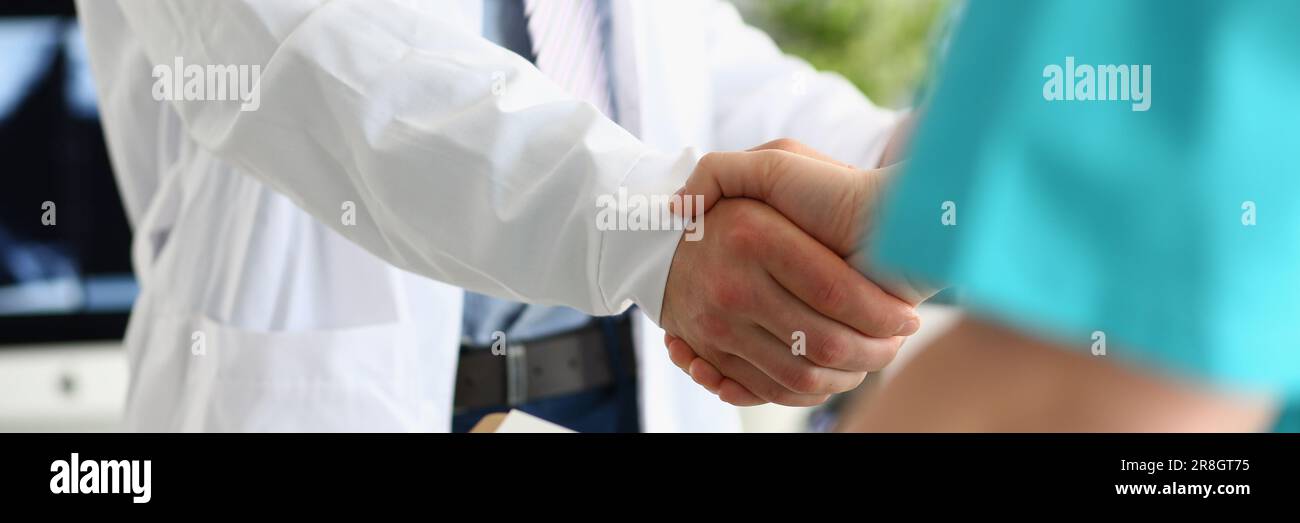 Closeup of two doctors shaking hands against backdrop of medical office ...