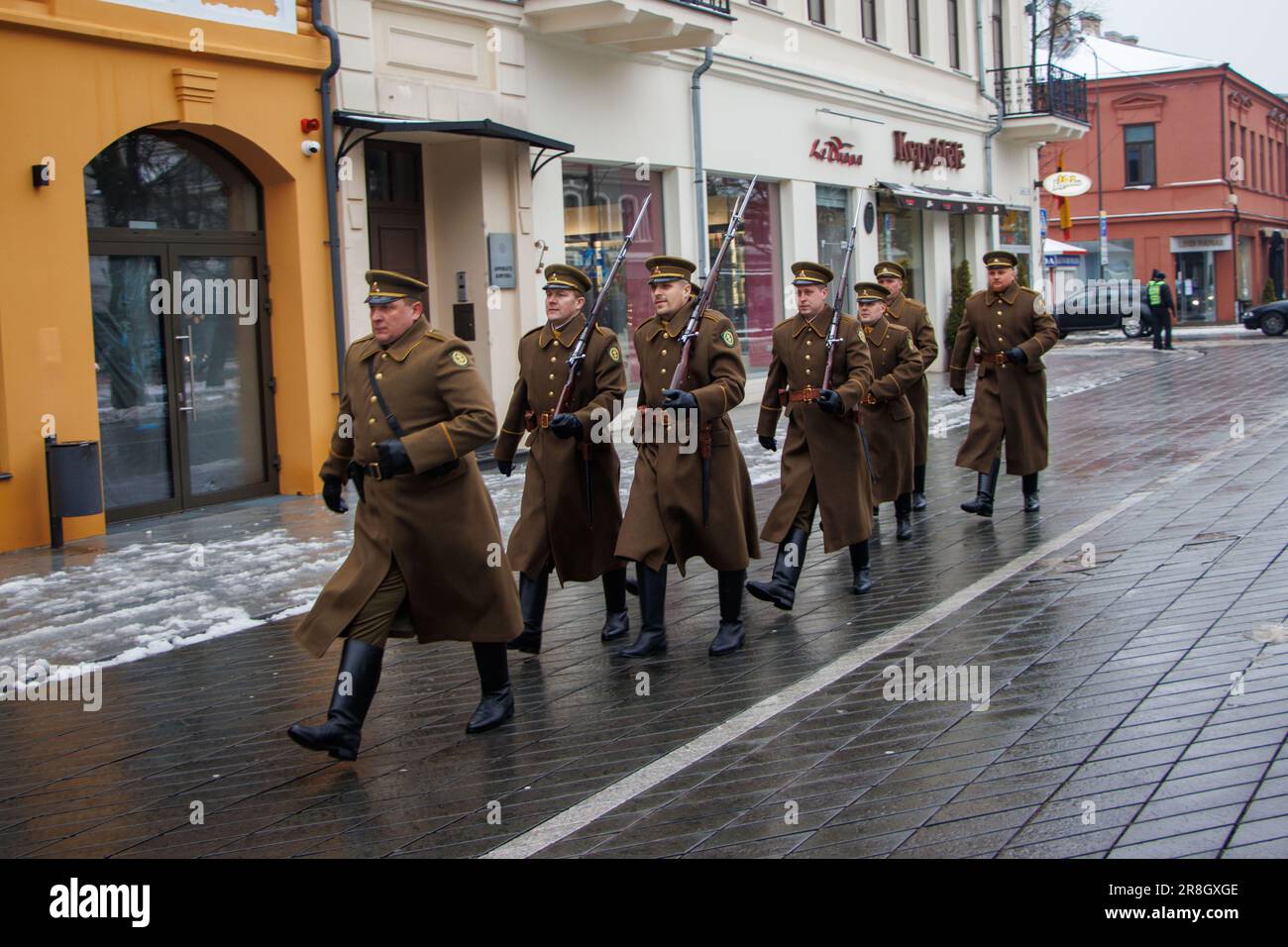 A group of uniformed men march in unison down a city street on ...