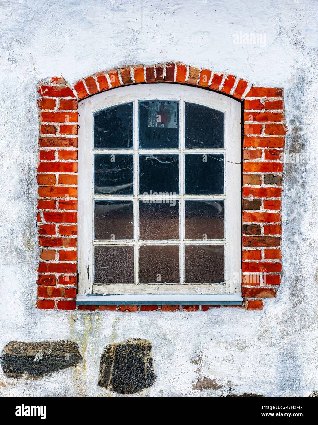 A close-up view of an old window with a brick frame set against a white ...