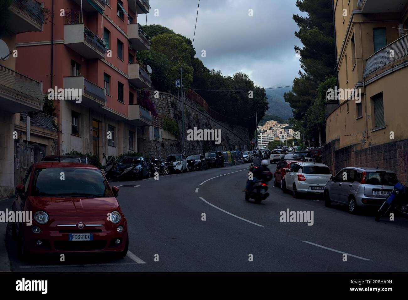 Sloping street with parked cars by its side and condominium bordering ...