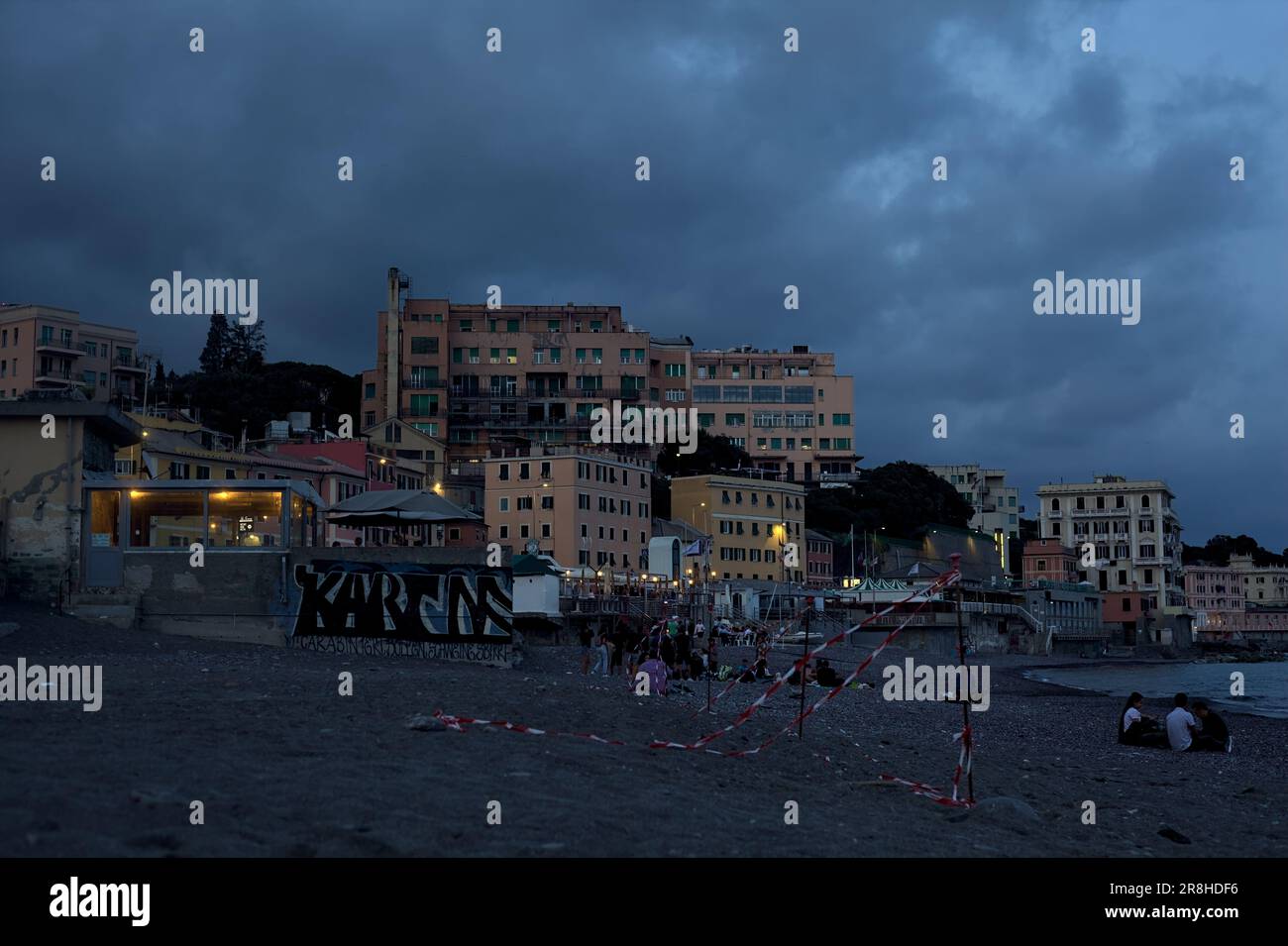 Beach with people sitting next to an italian town at dusk Stock Photo ...