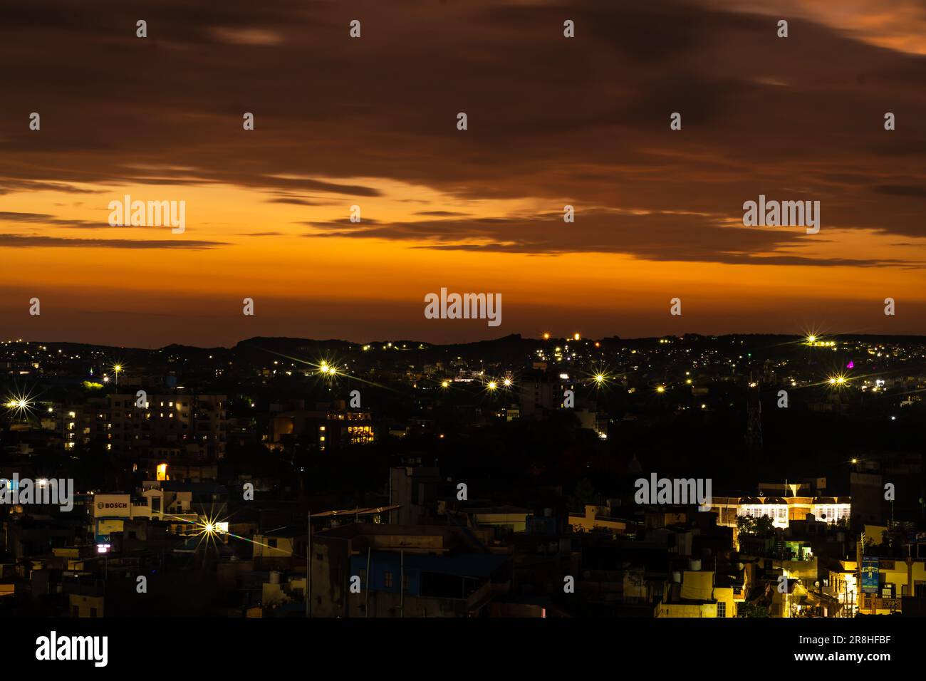 city night light view with dramatic sunset orange sky from mountain top ...