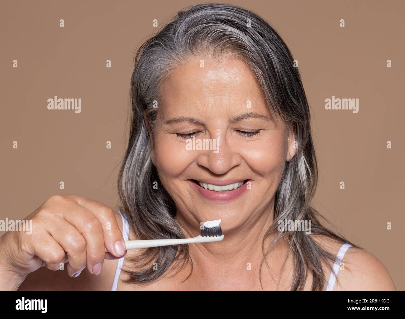 Smiling european senior grey-haired woman brushing her teeth with ...