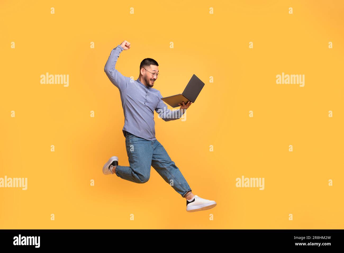 Emotional young asian man jumping up with laptop in hand Stock Photo ...