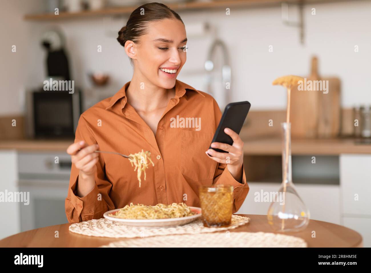 Happy european lady using smartphone and eating homemade pasta having ...