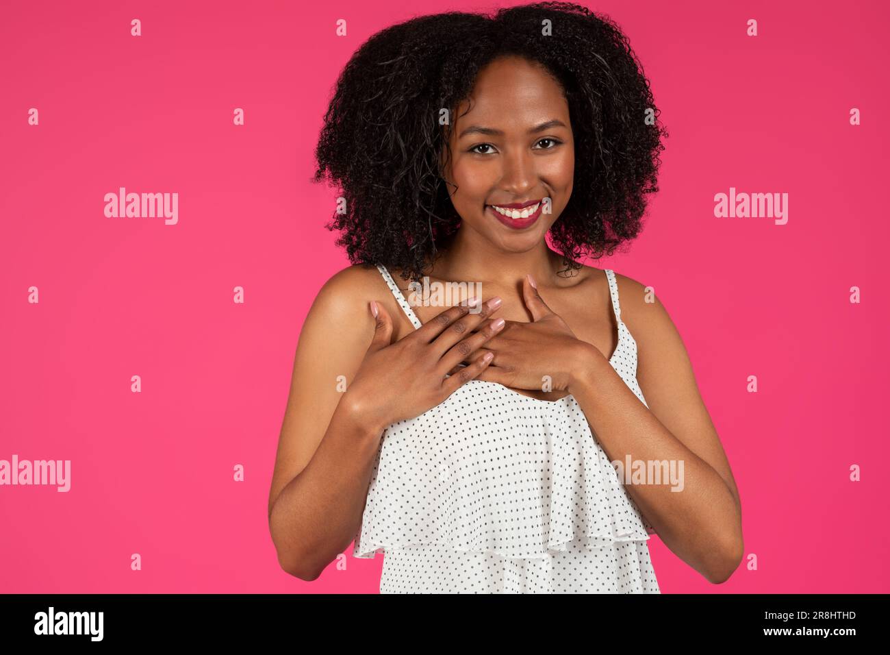 Glad young black curly lady presses hands to chest, makes sign of ...