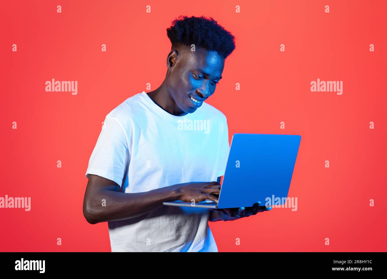 Happy african american man typing on laptop keyboard, red background ...