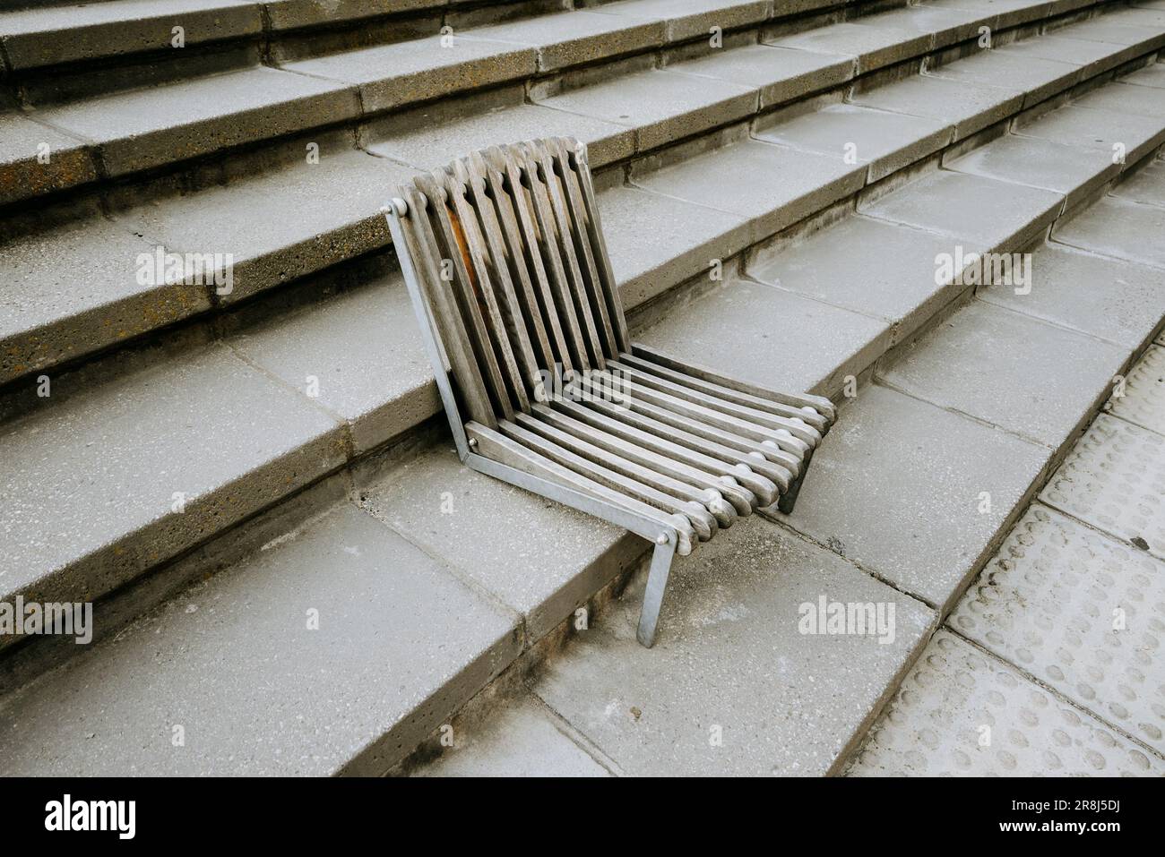 An aged, weathered chair is placed atop a set of concrete steps ...