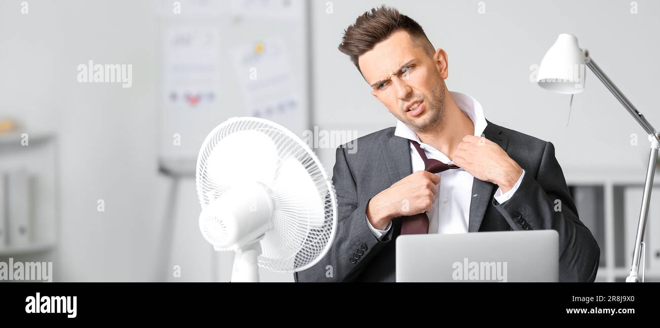Angry man suffering from heat near electric fan in office Stock Photo ...