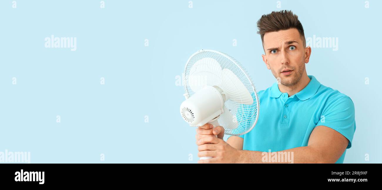 Confused man with electric fan on light blue background with space for ...