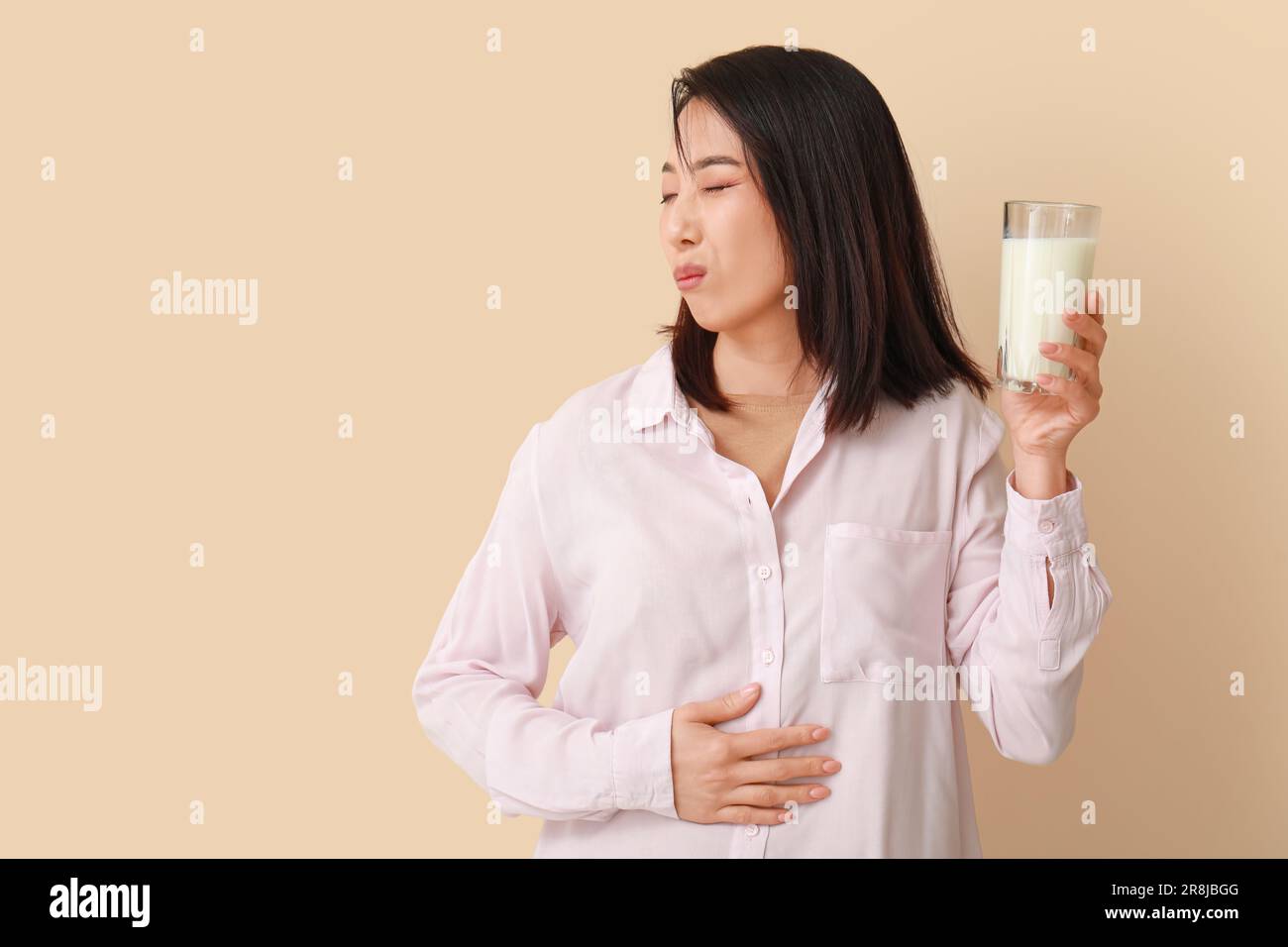 Young Asian woman with lactose intolerance on beige background Stock ...