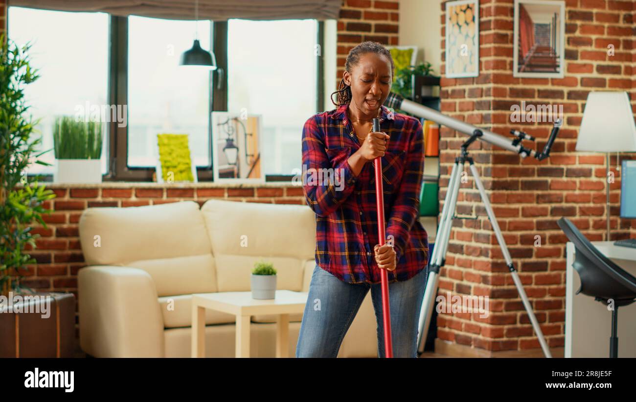 African american housewife listening to music and mopping apartment ...