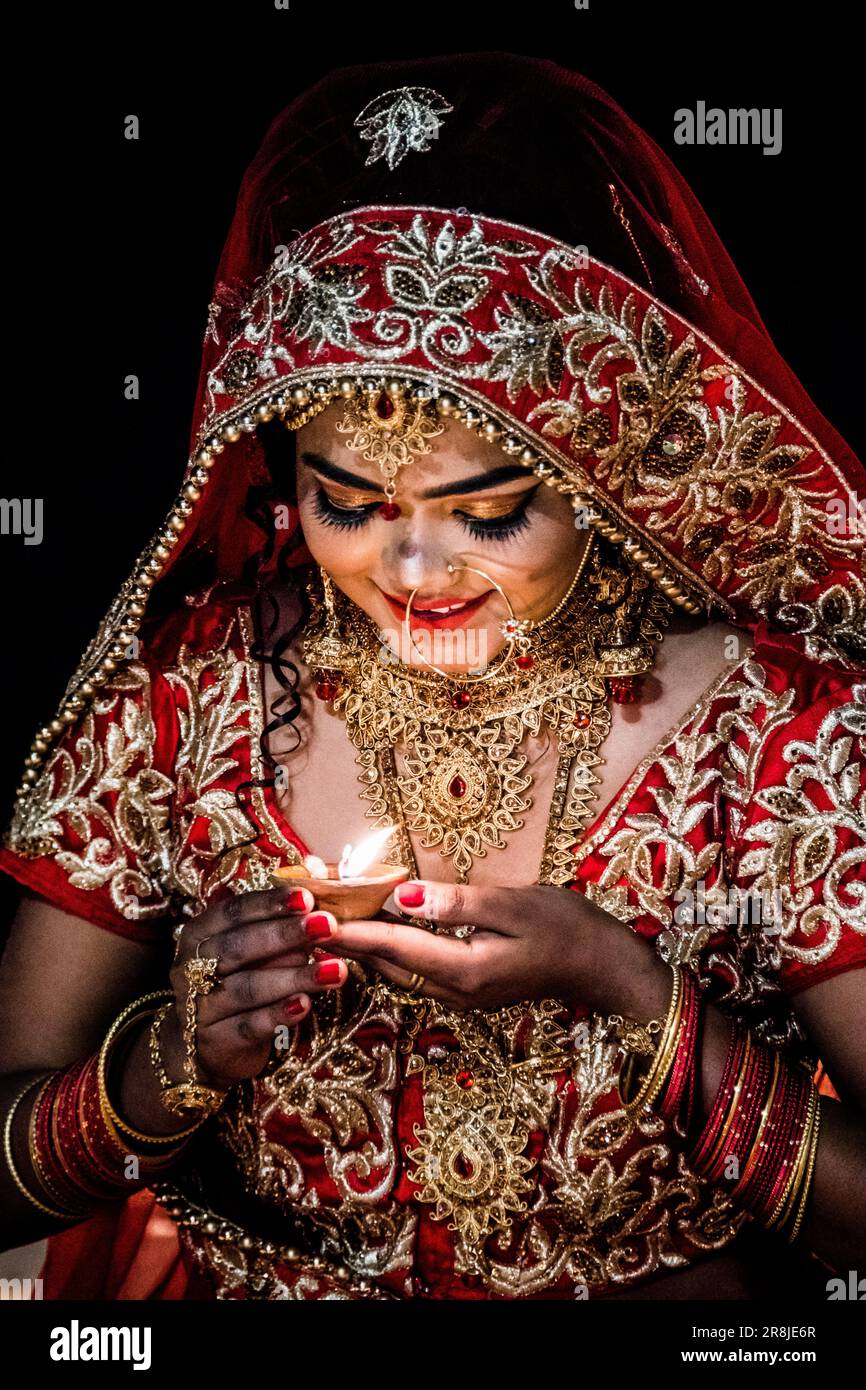 A young woman in a wedding sari poses with ghee lamps before dev ...