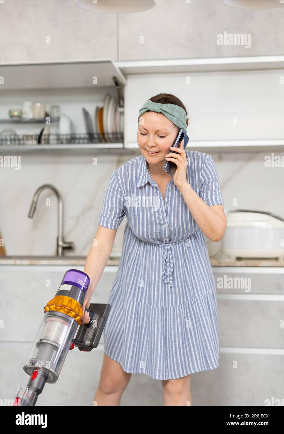 Housewife is cleaning the room - vacuuming and talking on smartphone at ...