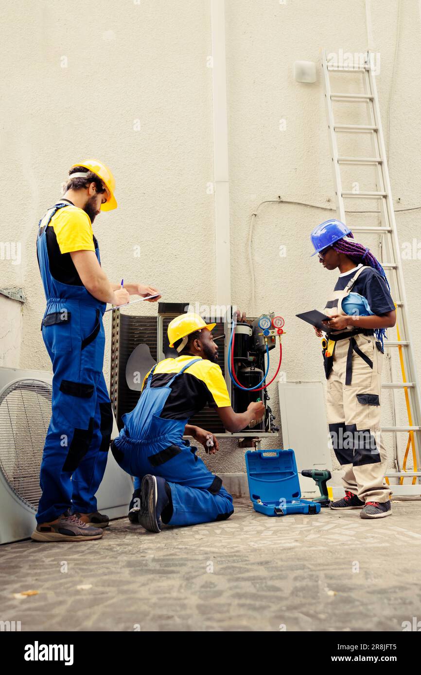 Diverse team of seasoned wiremen mending condenser unit electrical ...