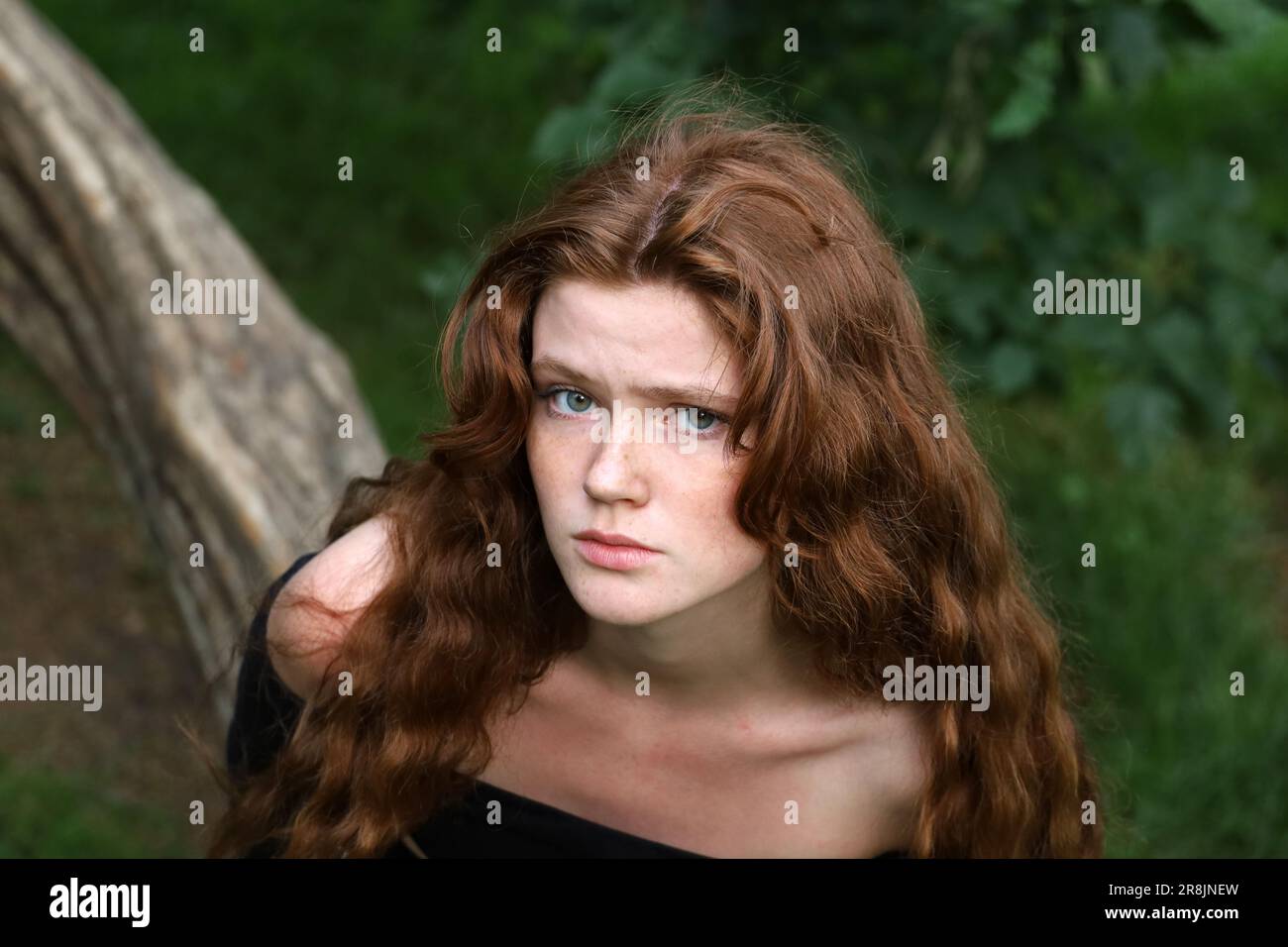 Portrait of upset girl with long red hair and freckles in summer park ...