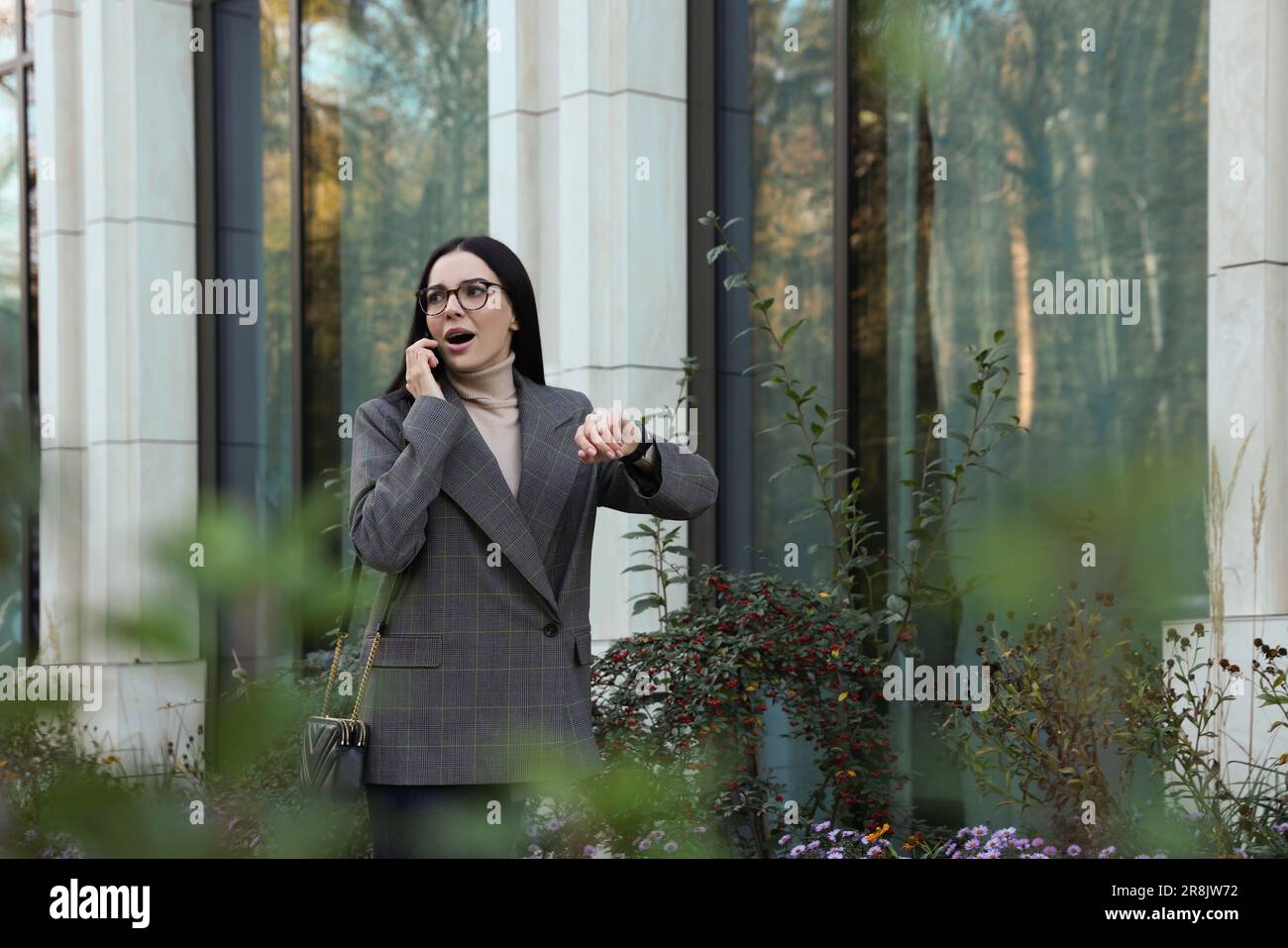 Emotional woman checking time while talking on smartphone outdoors ...