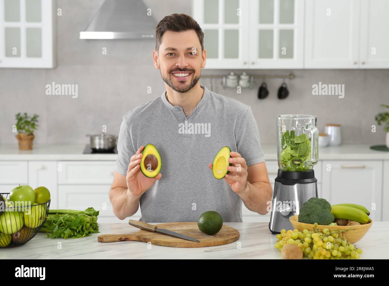 Man holding halves of avocado for delicious smoothie at white marble ...