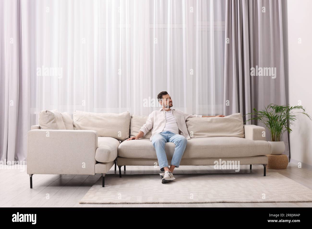 Happy man resting on sofa near window with beautiful curtains in living ...