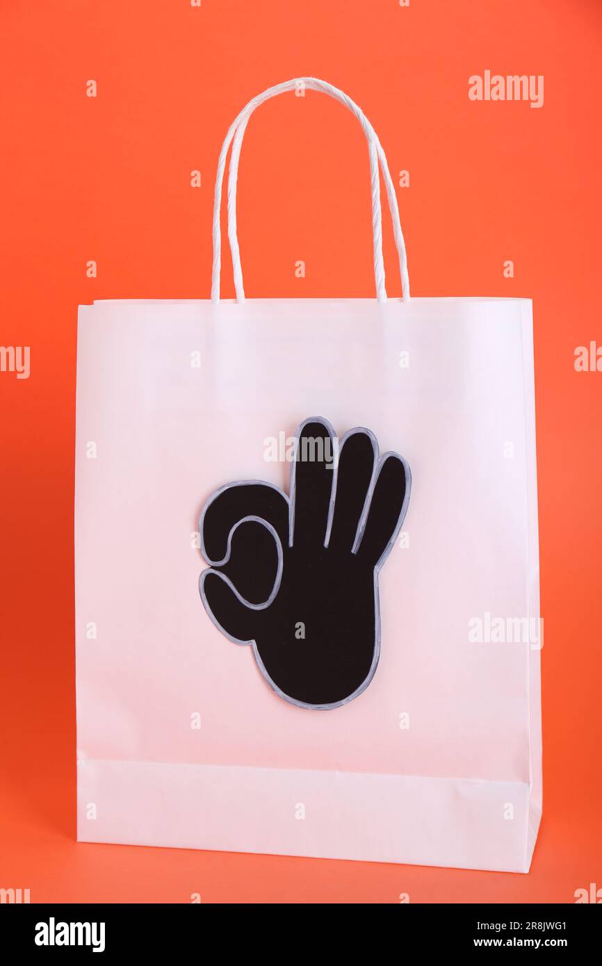 Paper bag and cutout of okay hand gesture on orange background Stock ...