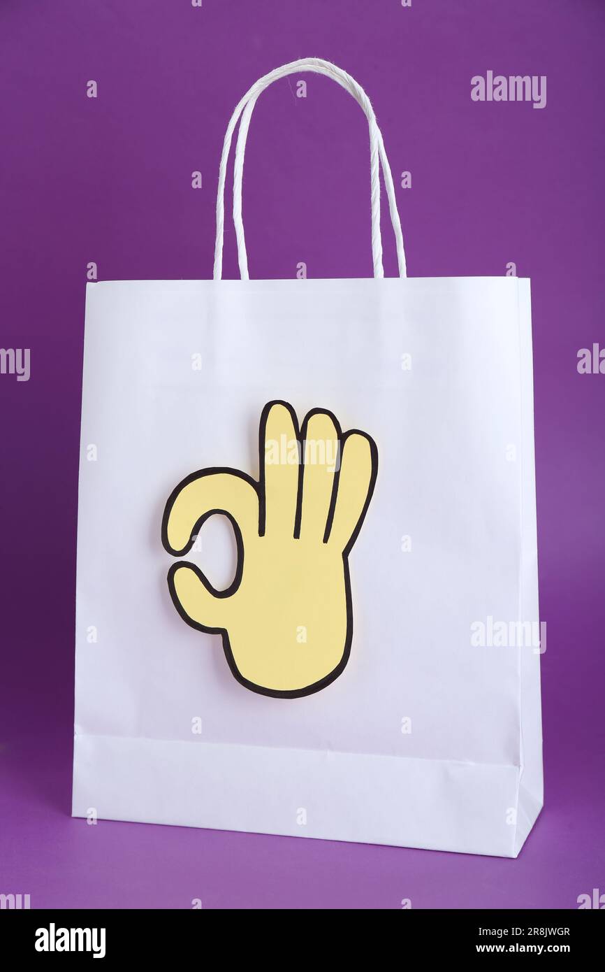 Paper bag and cutout of okay hand gesture on purple background Stock ...