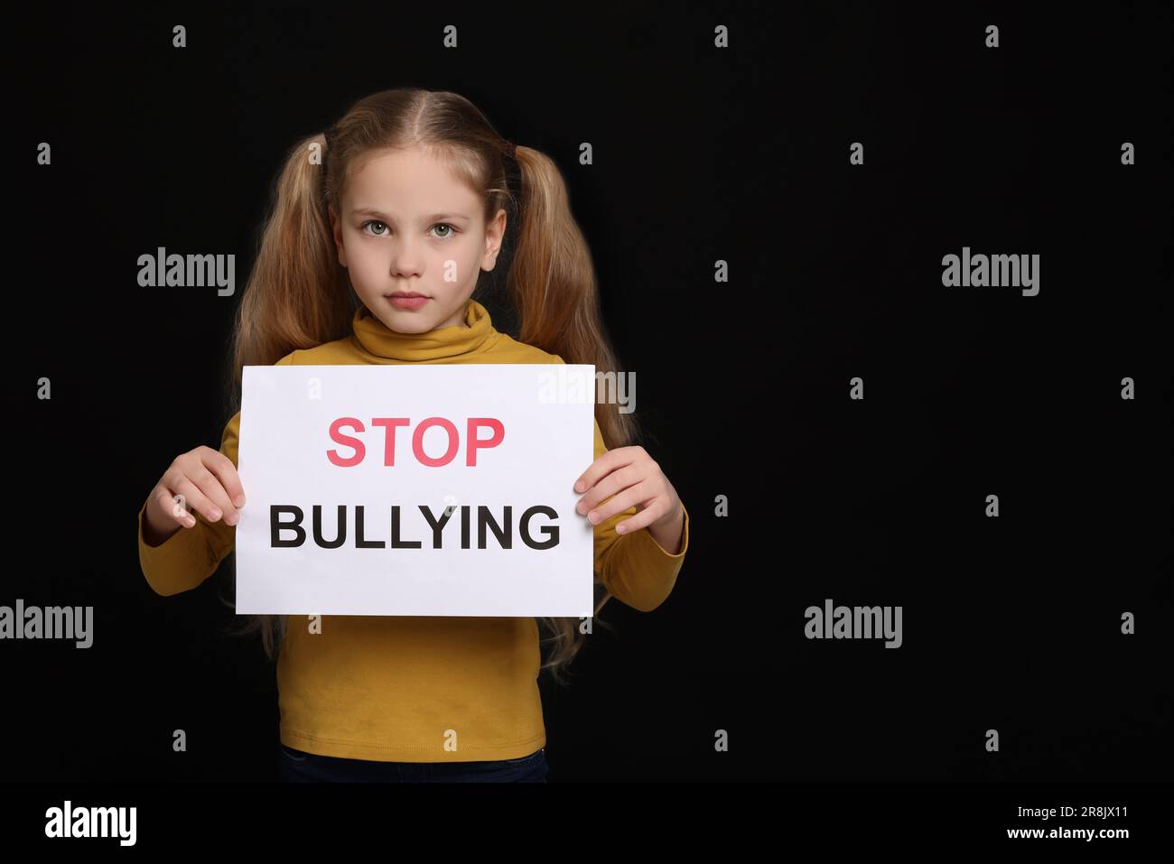 Girl holding sign with phrase Stop Bullying on black background, space ...