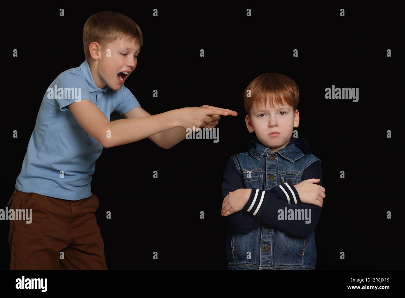 Boy laughing and pointing at upset kid on black background. Children's ...