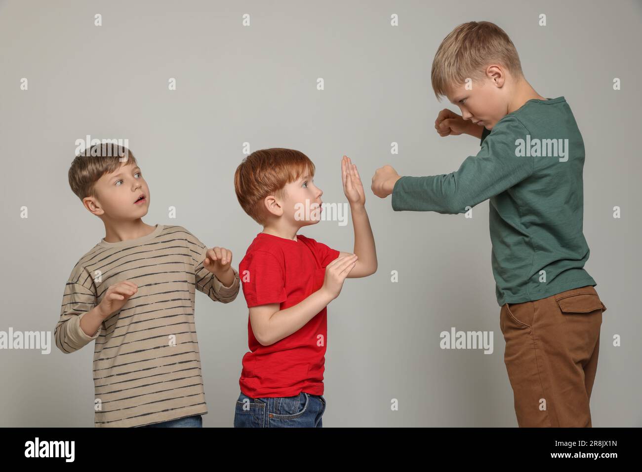 Boy with clenched fists bullying scared kids on light grey background ...