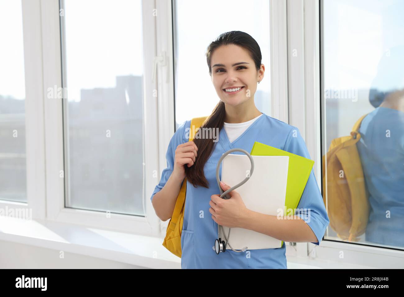 Smart medical student with stethoscope and folders in college hallway ...