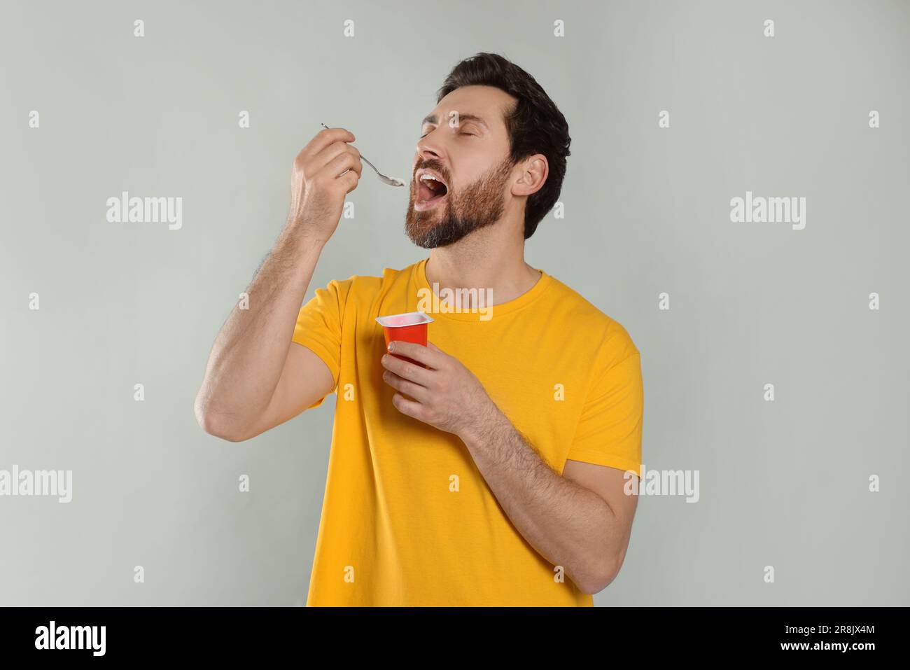 Handsome man eating delicious yogurt on light grey background Stock ...