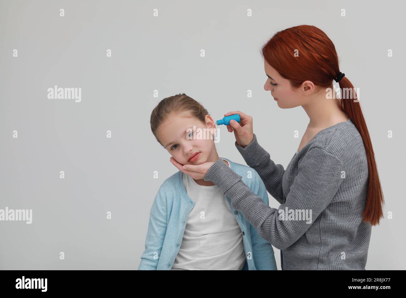 Mother Dripping Medication Into Daughters Ear On Light Grey Background