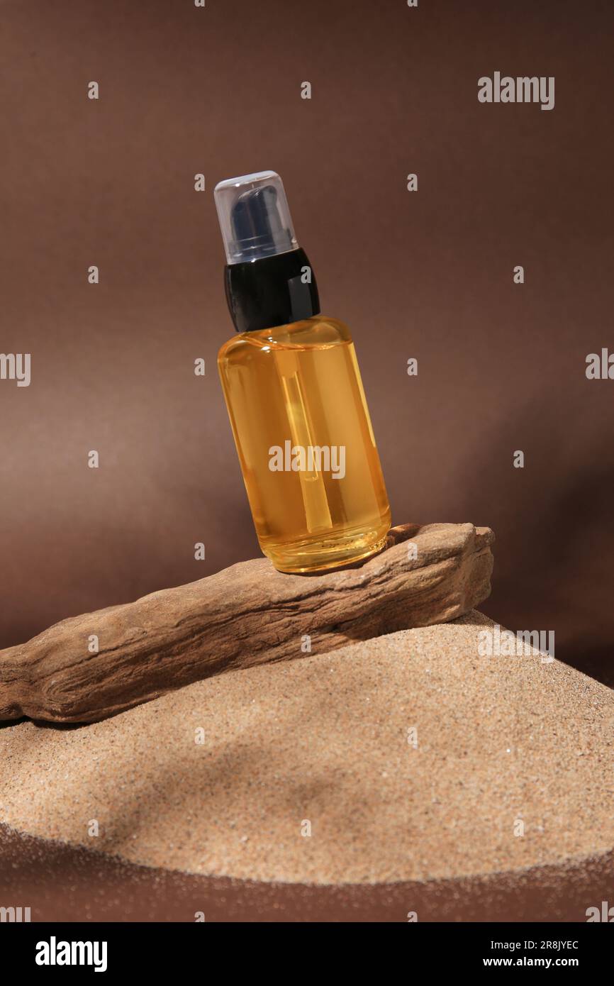Bottle of serum and tree bark on sand against brown background Stock ...