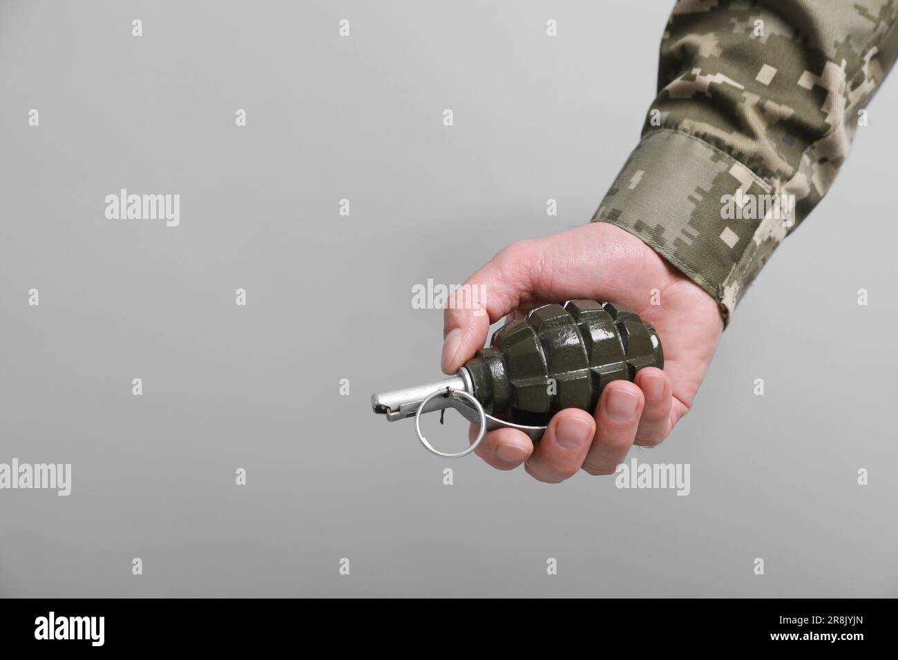 Soldier holding hand grenade on light grey background, closeup with ...