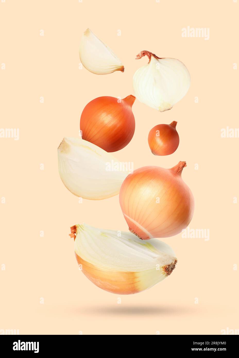Cut and whole onions falling on beige background Stock Photo - Alamy